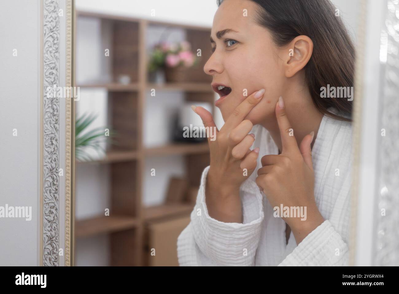 A distressed woman gazes into the bathroom mirror, feeling unhappy about her skin concerns Stock ...