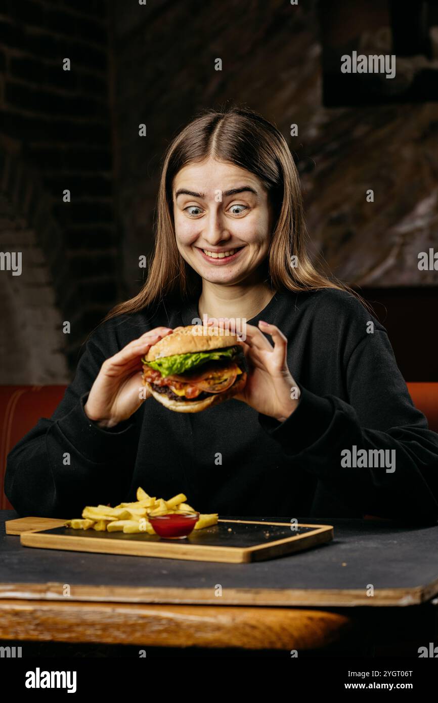 Playful woman enjoying a classic burger with fries and ketchup, perfect ...