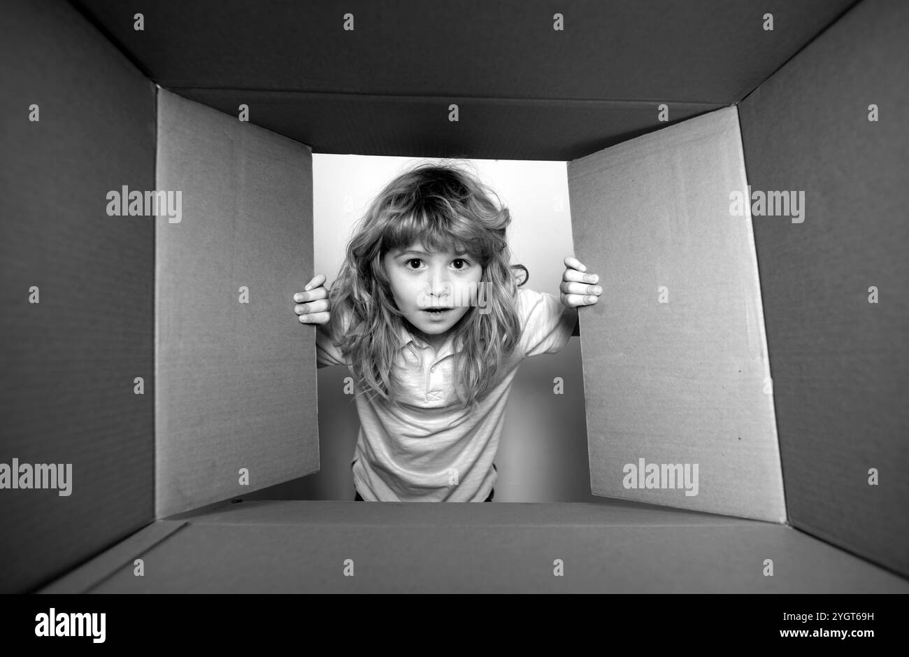 Funny child boy is opening gift and looking inside cardboard box ...