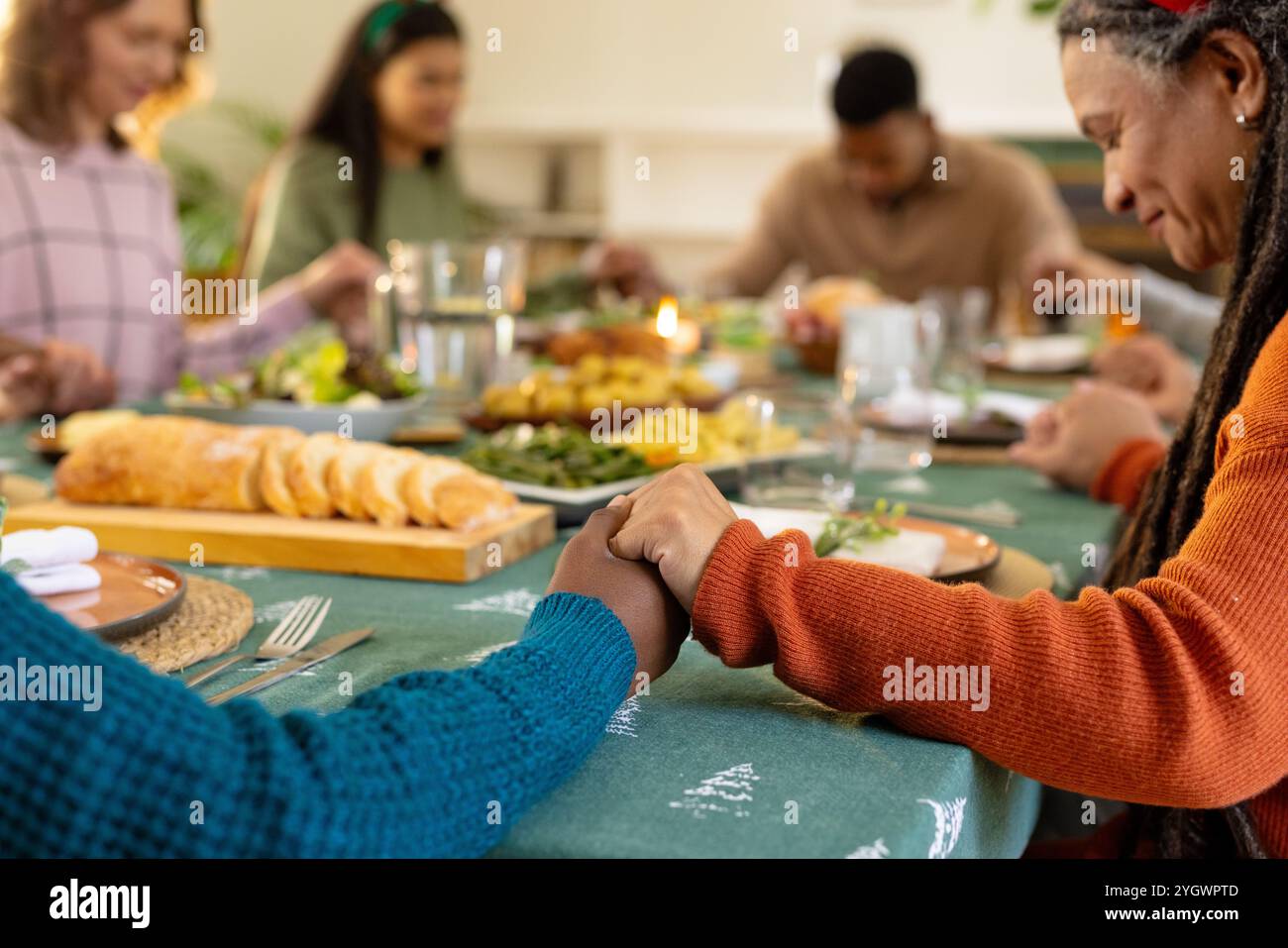 Christmas time, multiracial family holding hands around festive dinner ...