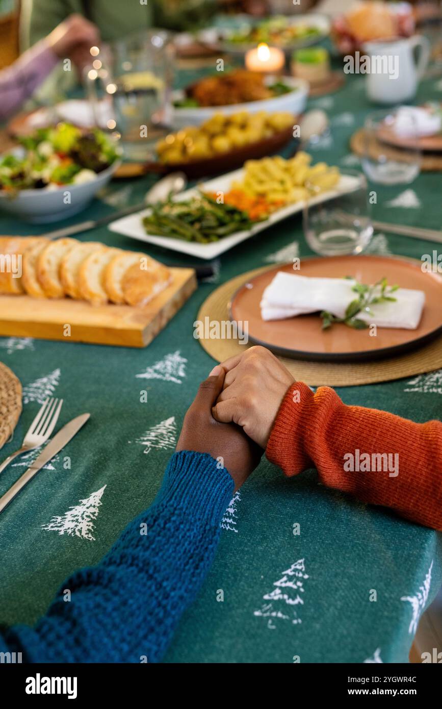 Christmas time, multiracial family holding hands at festive dinner ...