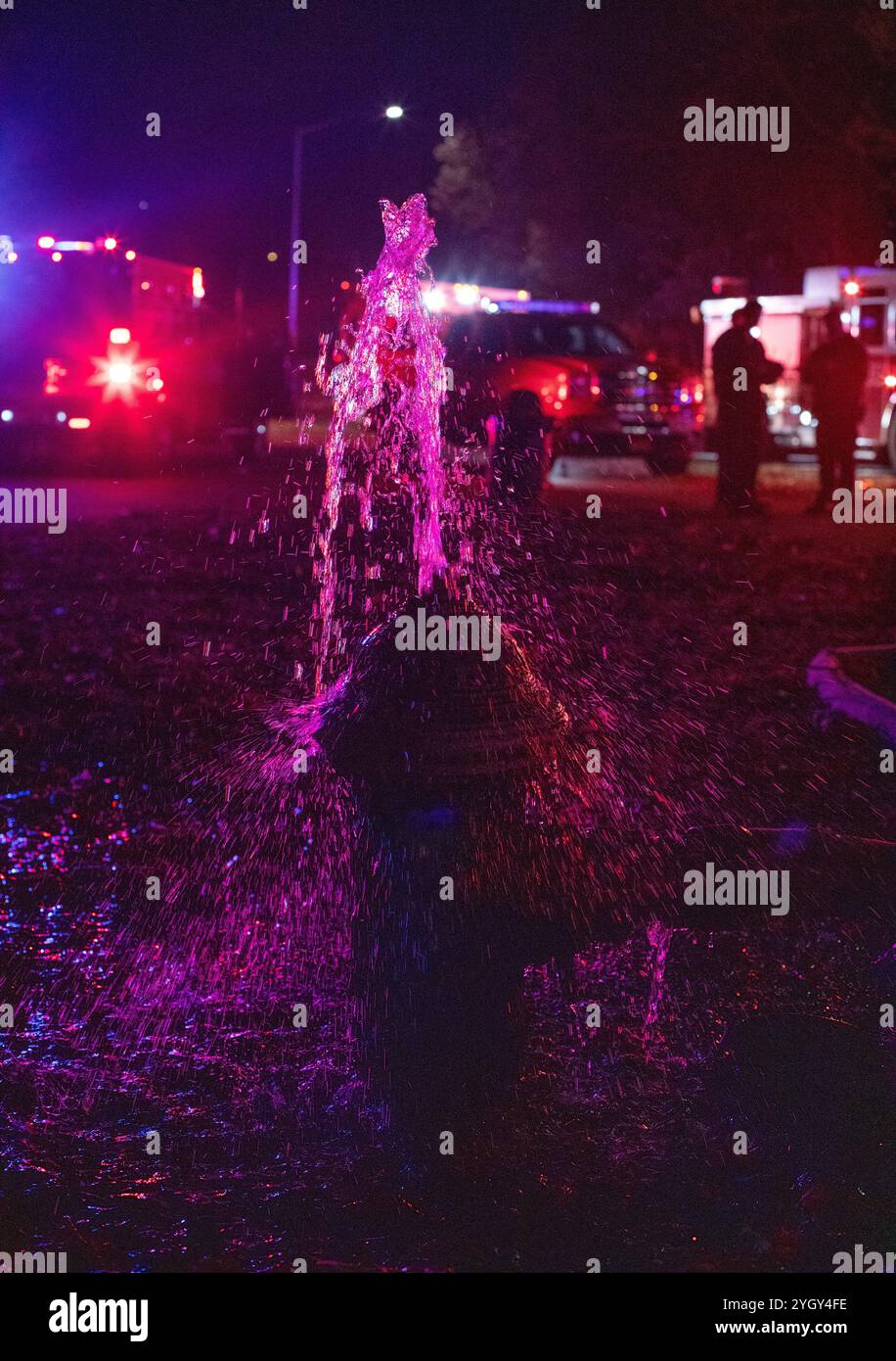 A fire hydrant leaks water with emergency vehicles in the background as ...