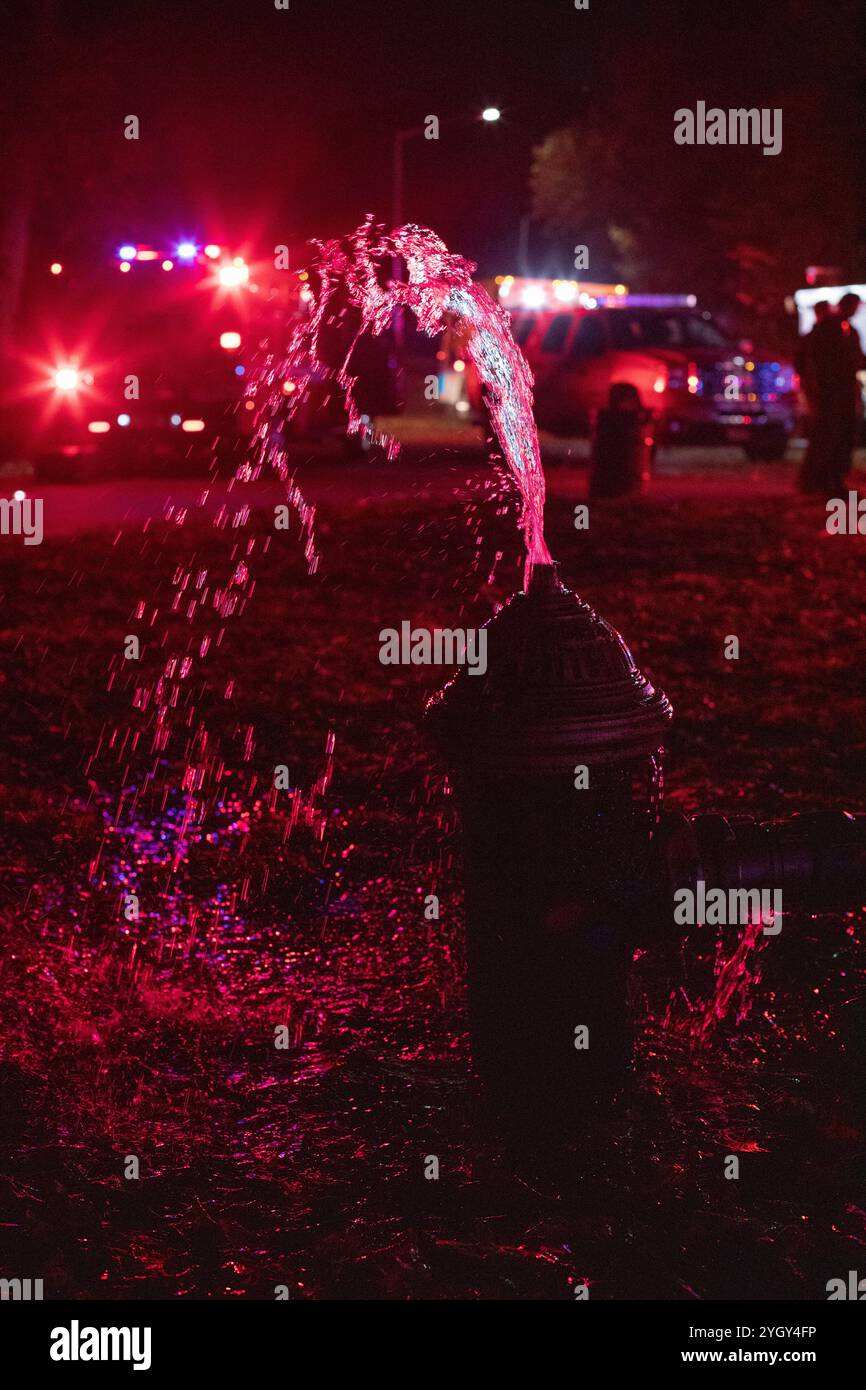 A fire hydrant leaks water with emergency vehicles in the background as ...