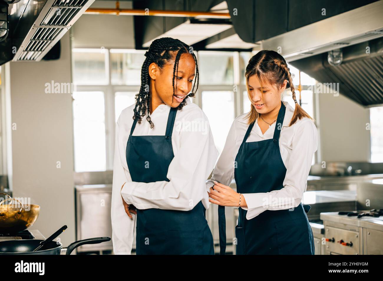In a restaurant kitchen a girlfriend chef assists her friend in tying ...