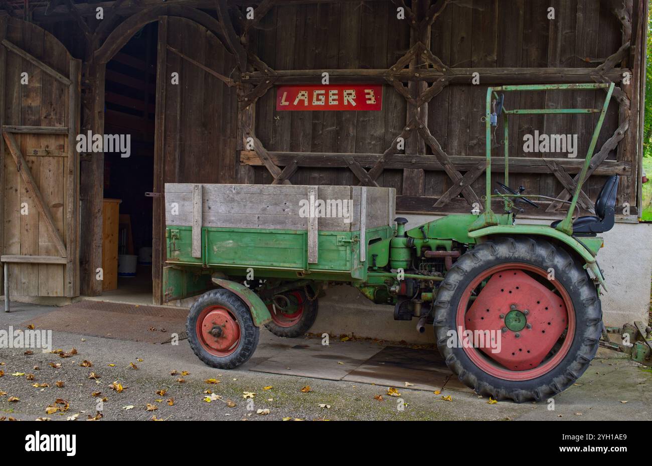 Old tractor in green with red wheels in front of a a wooden farmstead ...