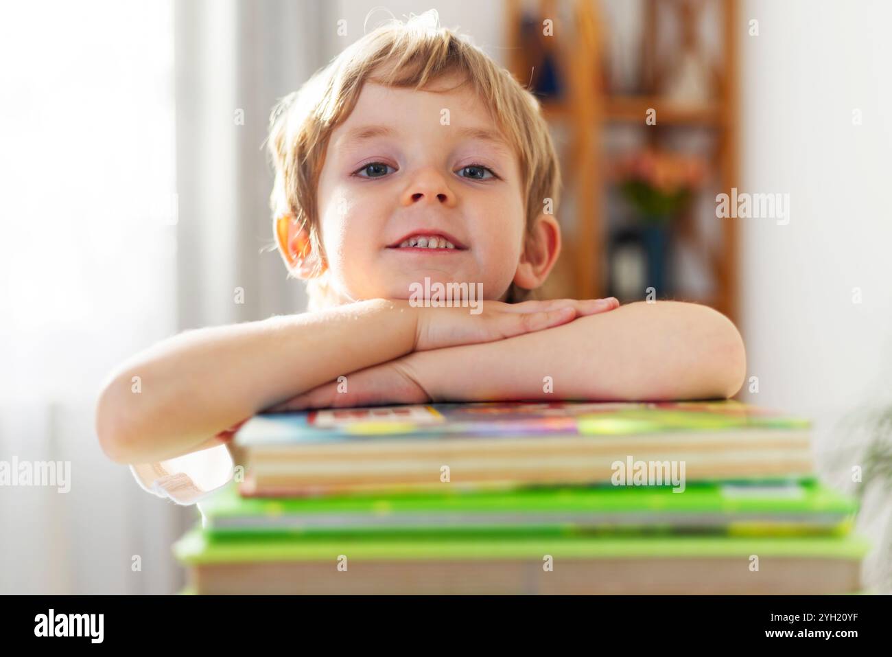 Smiling child resting on book stack Stock Photo - Alamy