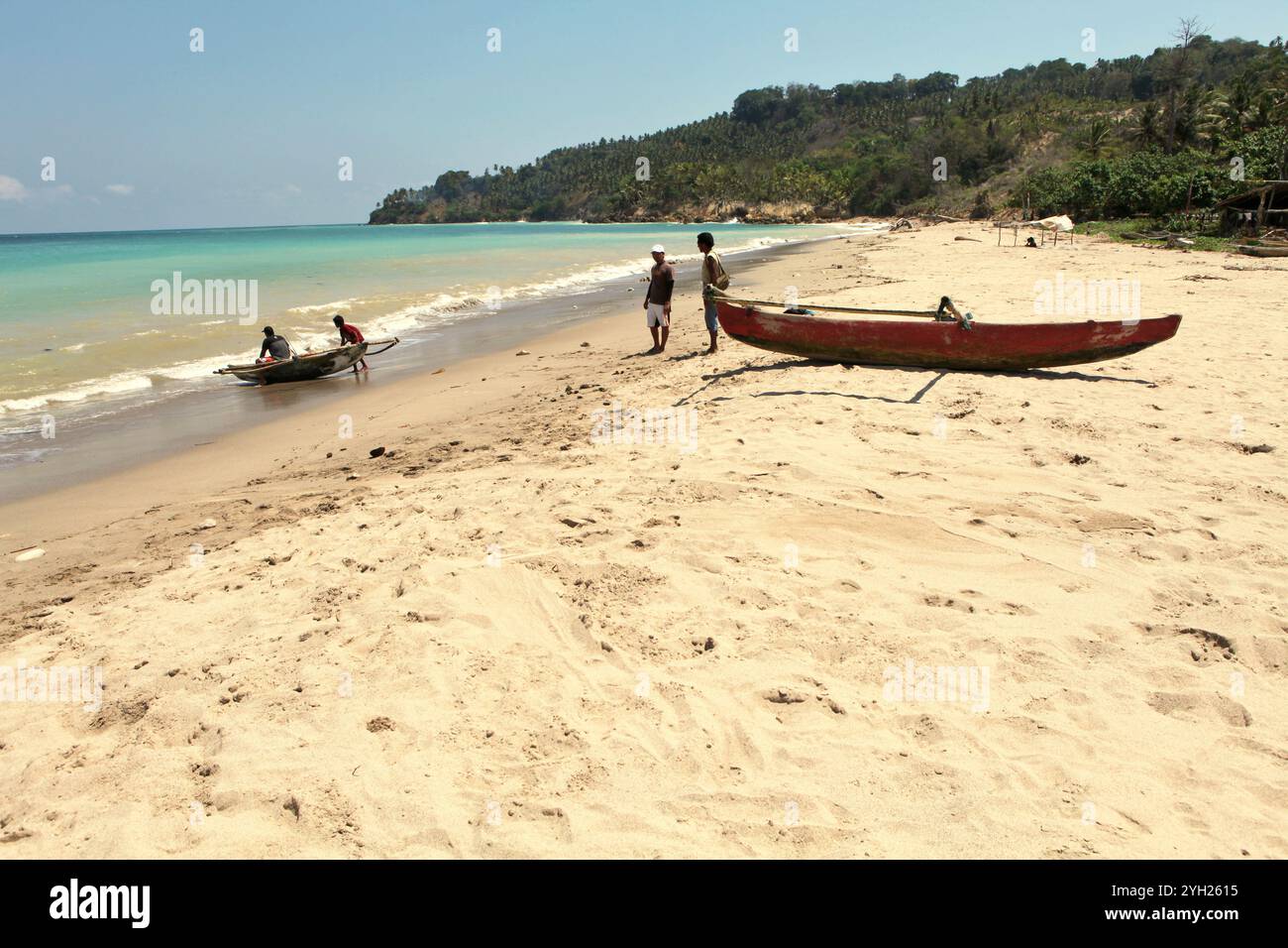 Traditional fishermen launch a fishing canoe onto the seawater in ...