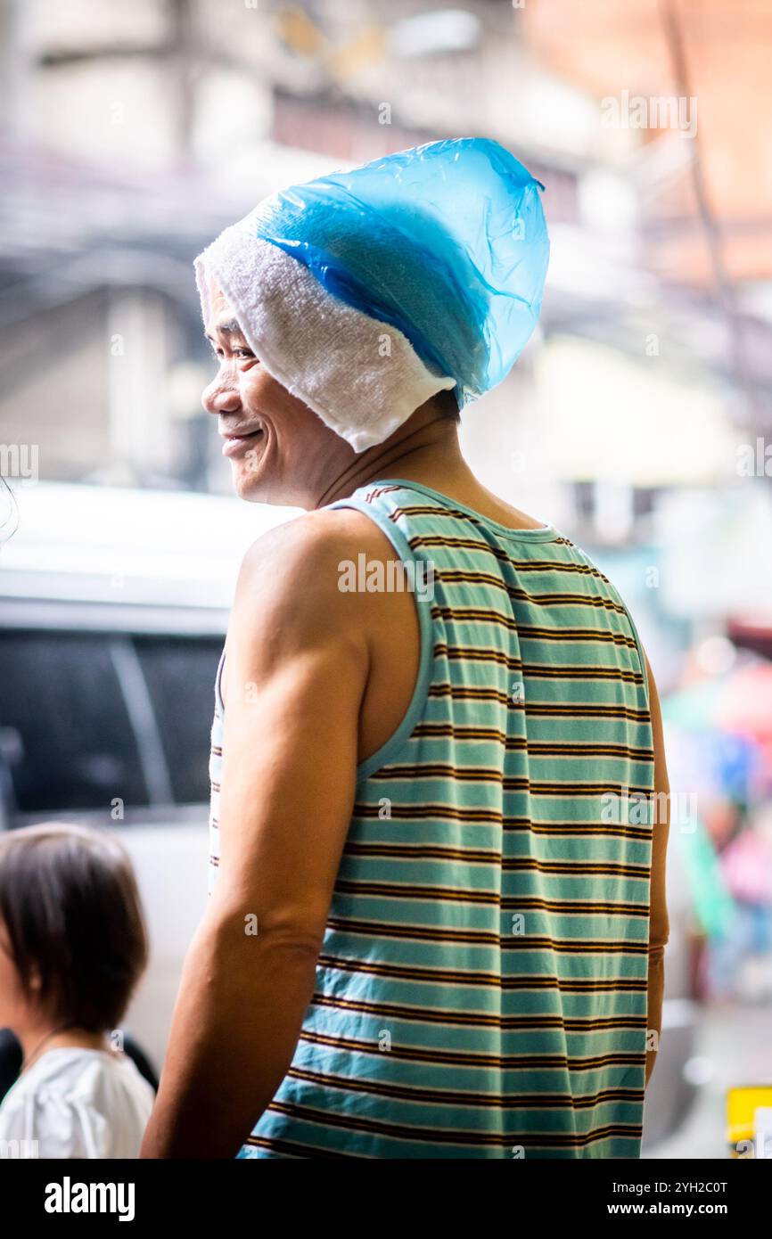 A Filipino market worker wears a plastic bag on his head to keep the ...