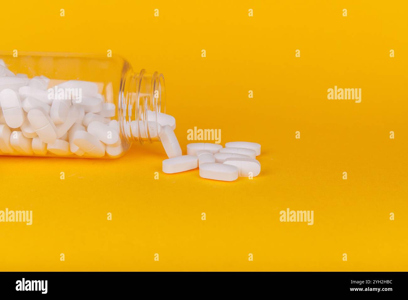A transparent pill bottle with white tablets on a yellow surface ...