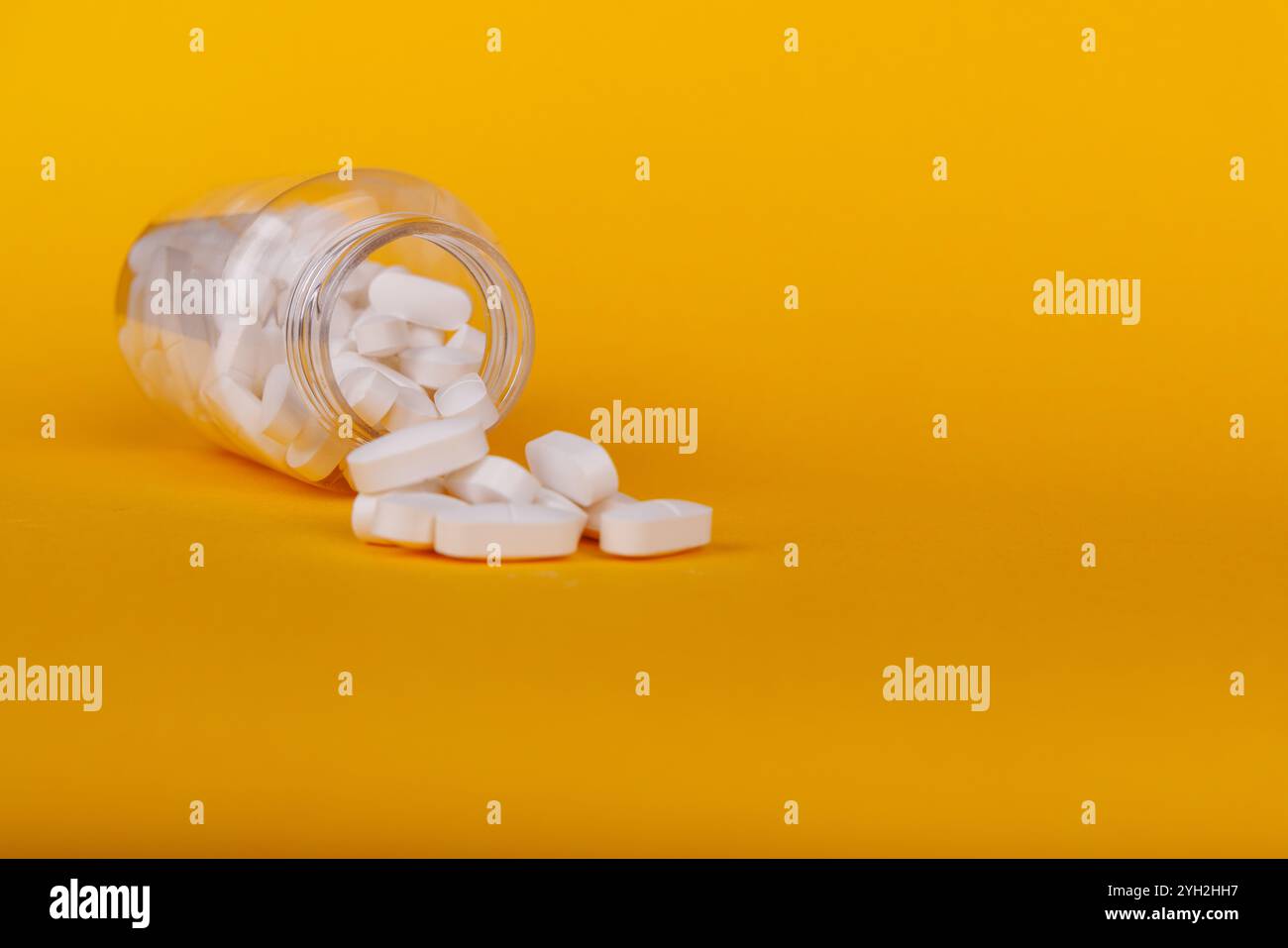 Clear pill bottle with white tablets on yellow background, focusing on ...