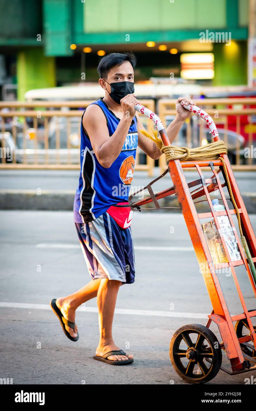A Filipino market worker pushes his trolley along the street in a ...
