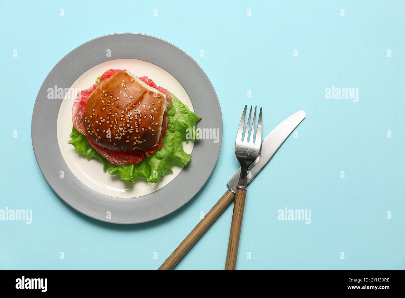 Plate with tasty burger and plastic on blue background. Microplastic ...