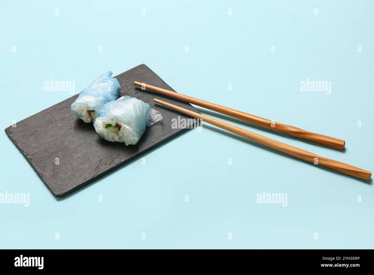 Tasty sushi rolls with plastic on plate against blue background ...