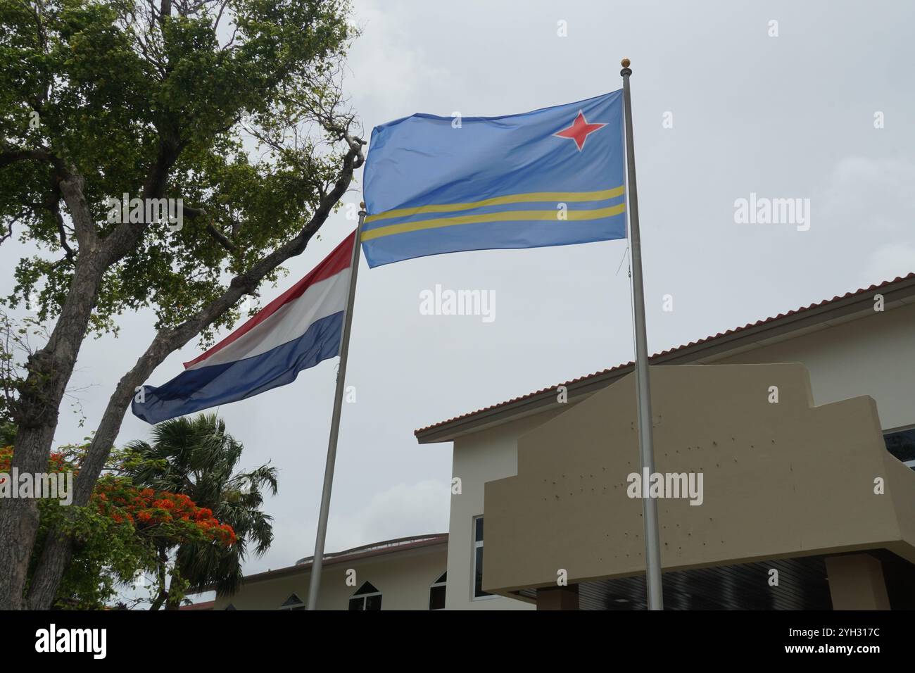 Aruba flag and Netherland flag are on metal poles and blow in the wind ...
