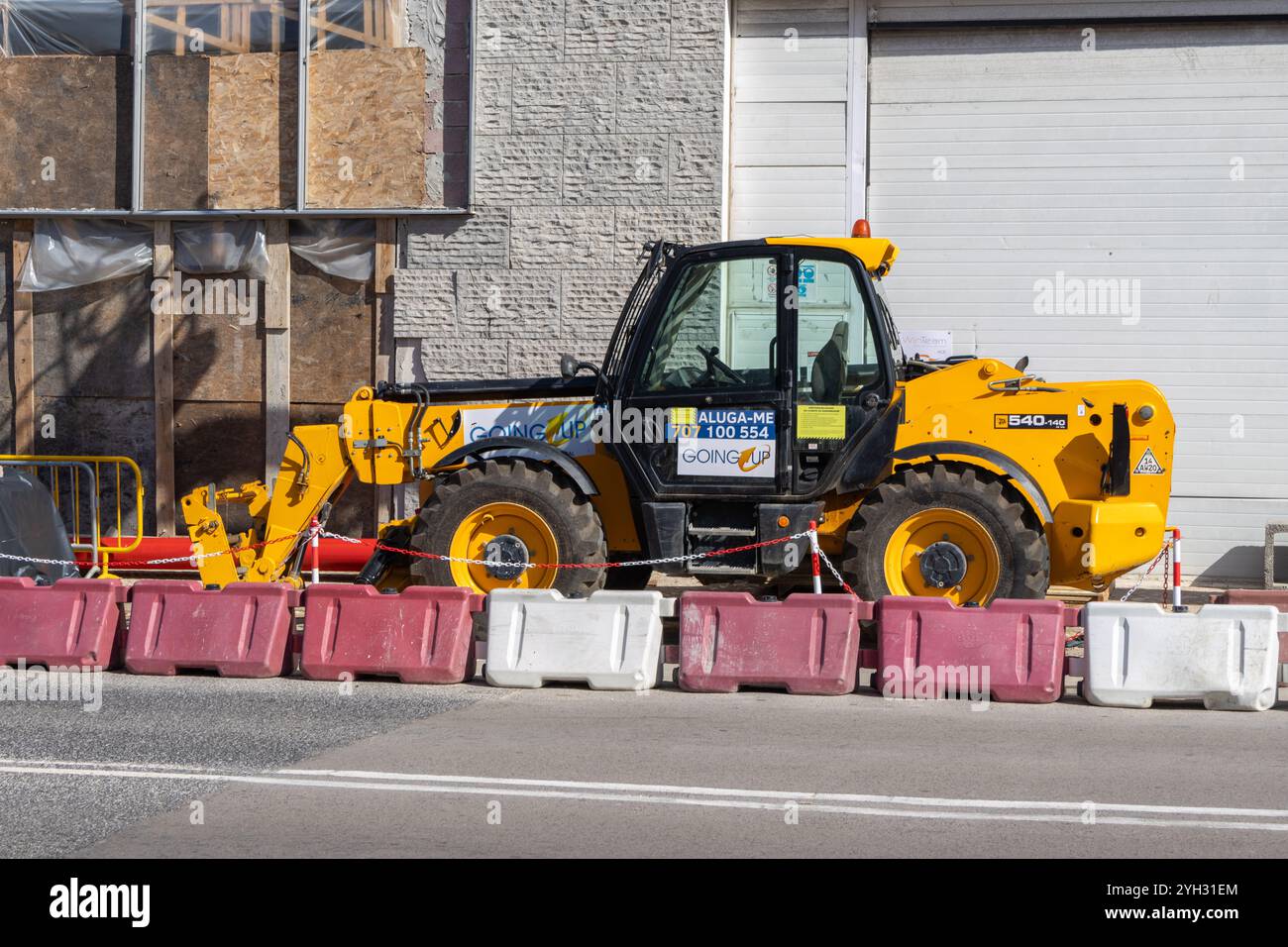 Yellow telescopic handler parked on a city street next to a ...