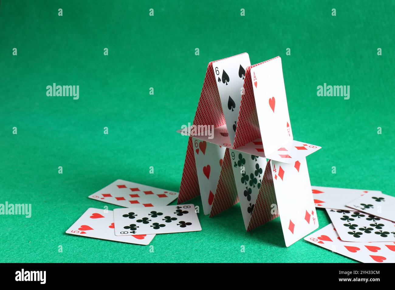 Collapsed house of playing cards on green background. Space for text ...