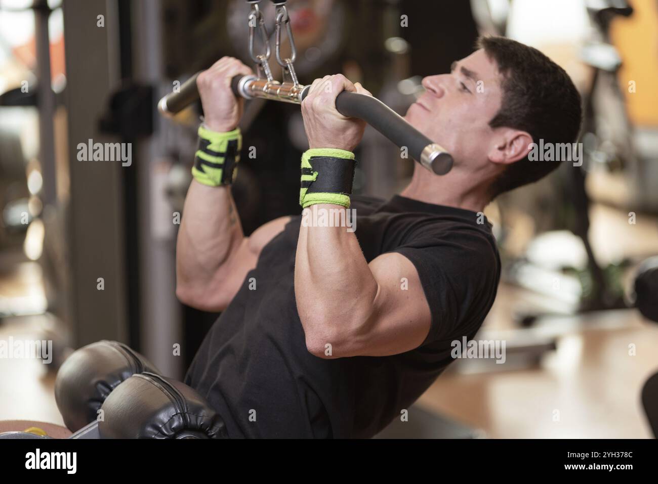 Cheerful guy training dorsal muscles by taking handles and bringing ...