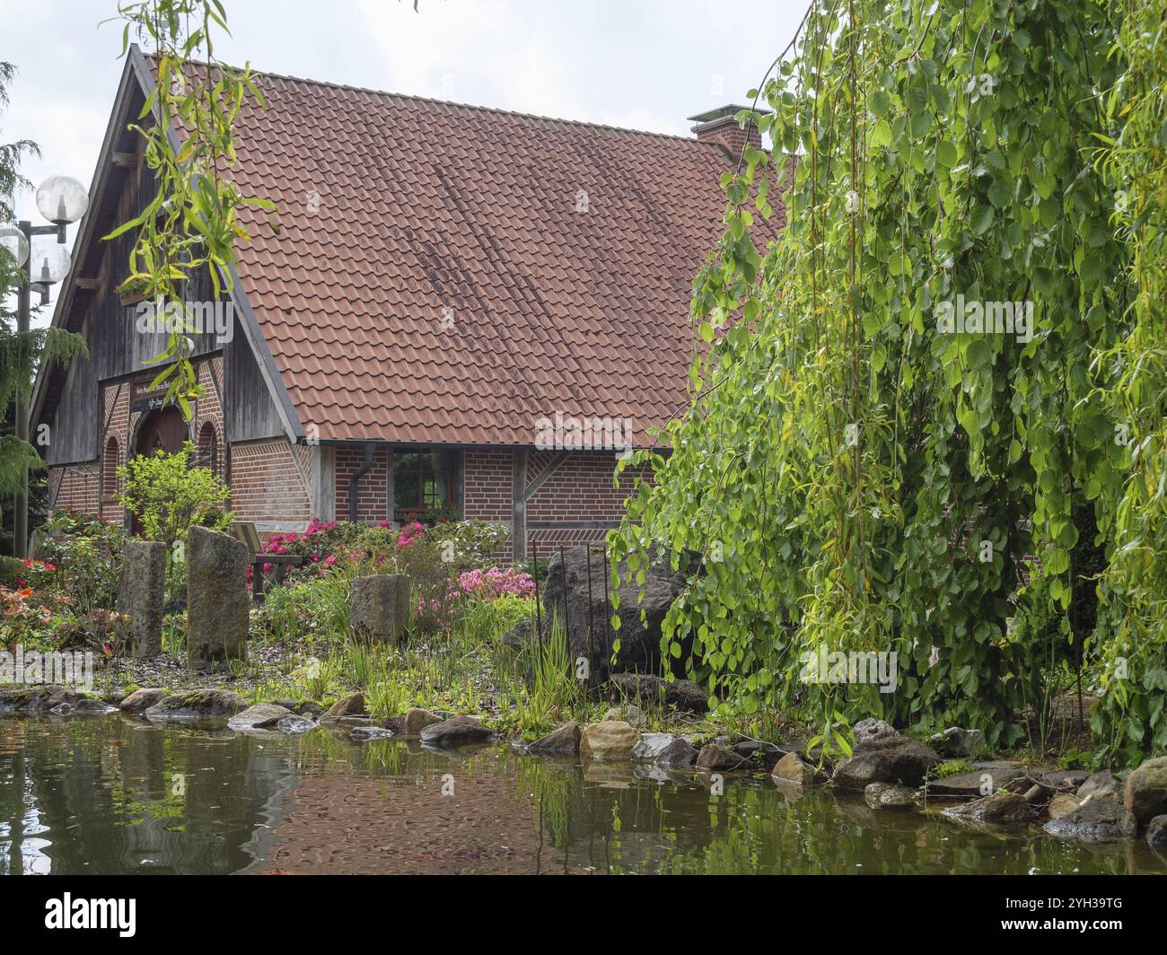 Traditional brick house next to a pond, surrounded by flowering shrubs ...