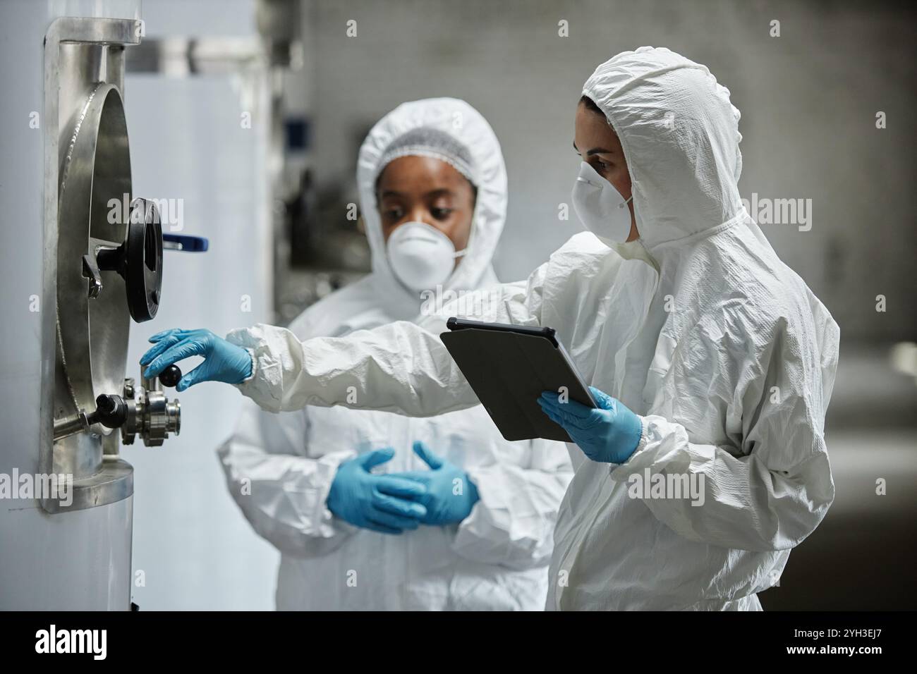 Side view of female process technician in hazmat suit using tablet ...