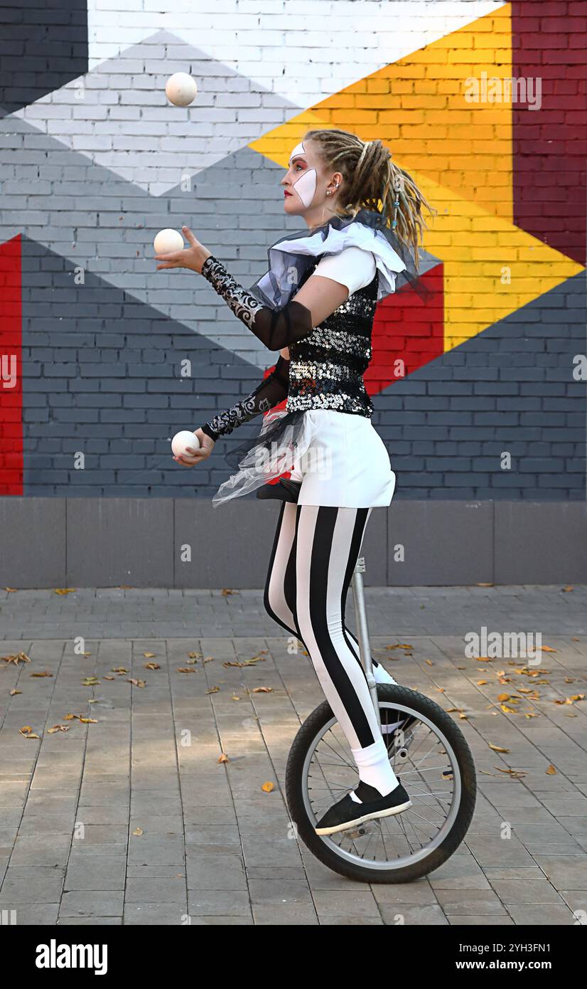Girl clown rides a unicycle and juggles balls in front of colorful wall outdoors Stock Photo - Alamy