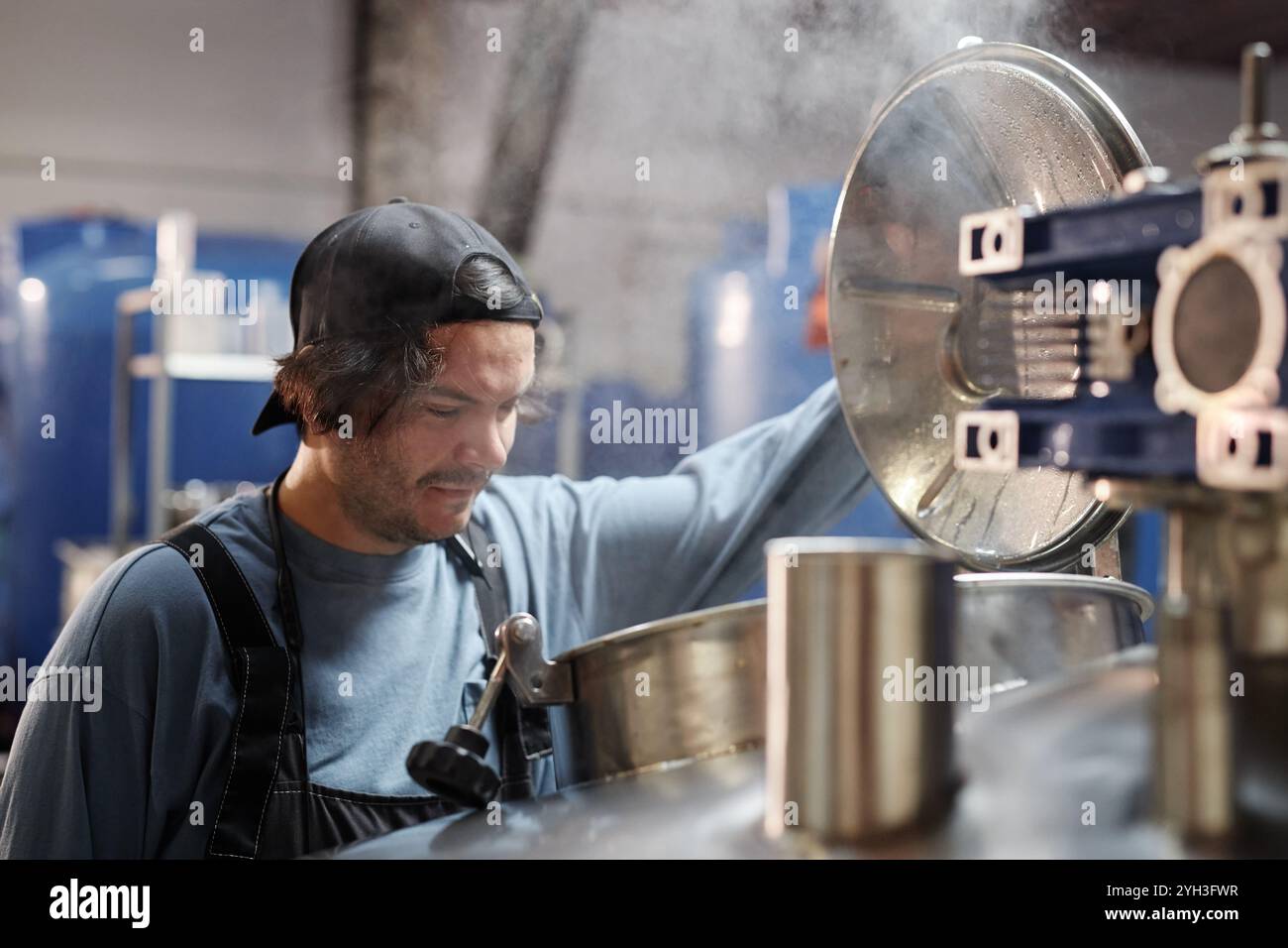 Medium shot of male cider production worker opening lid of stainless ...