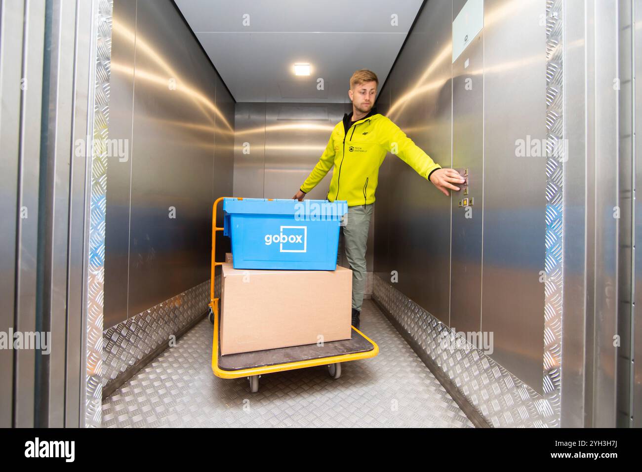 Man inside an elevator with a cart carrying a blue storage box and a ...