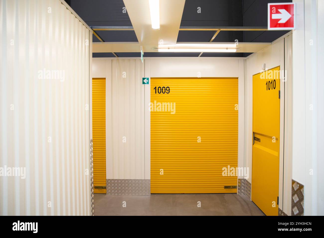 Storage facility corridor with numbered yellow roll-up doors and bright ...