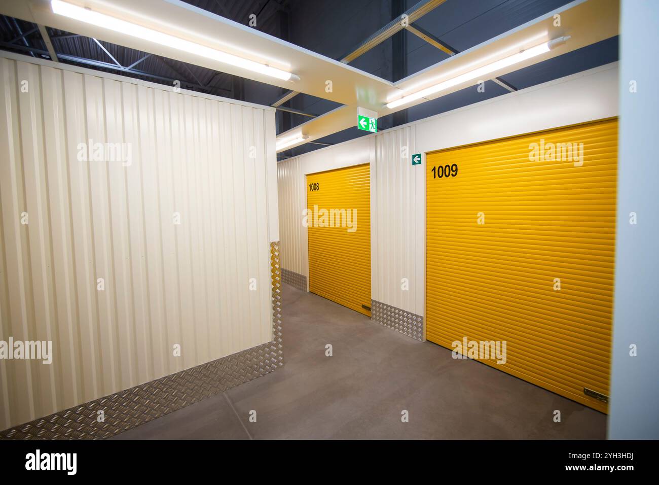 Storage facility corridor with numbered yellow roll-up doors and bright ...