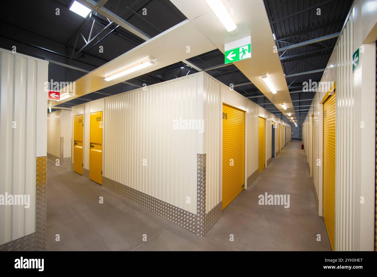 Storage facility corridor with numbered yellow roll-up doors and bright ...