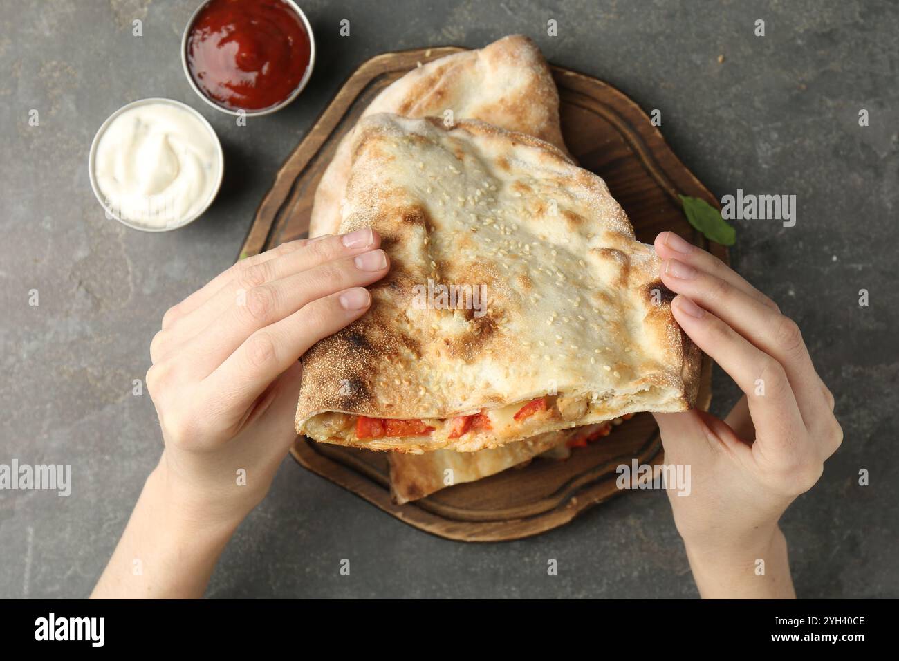 Woman eating tasty calzone with meat, cheese and tomato at grey ...