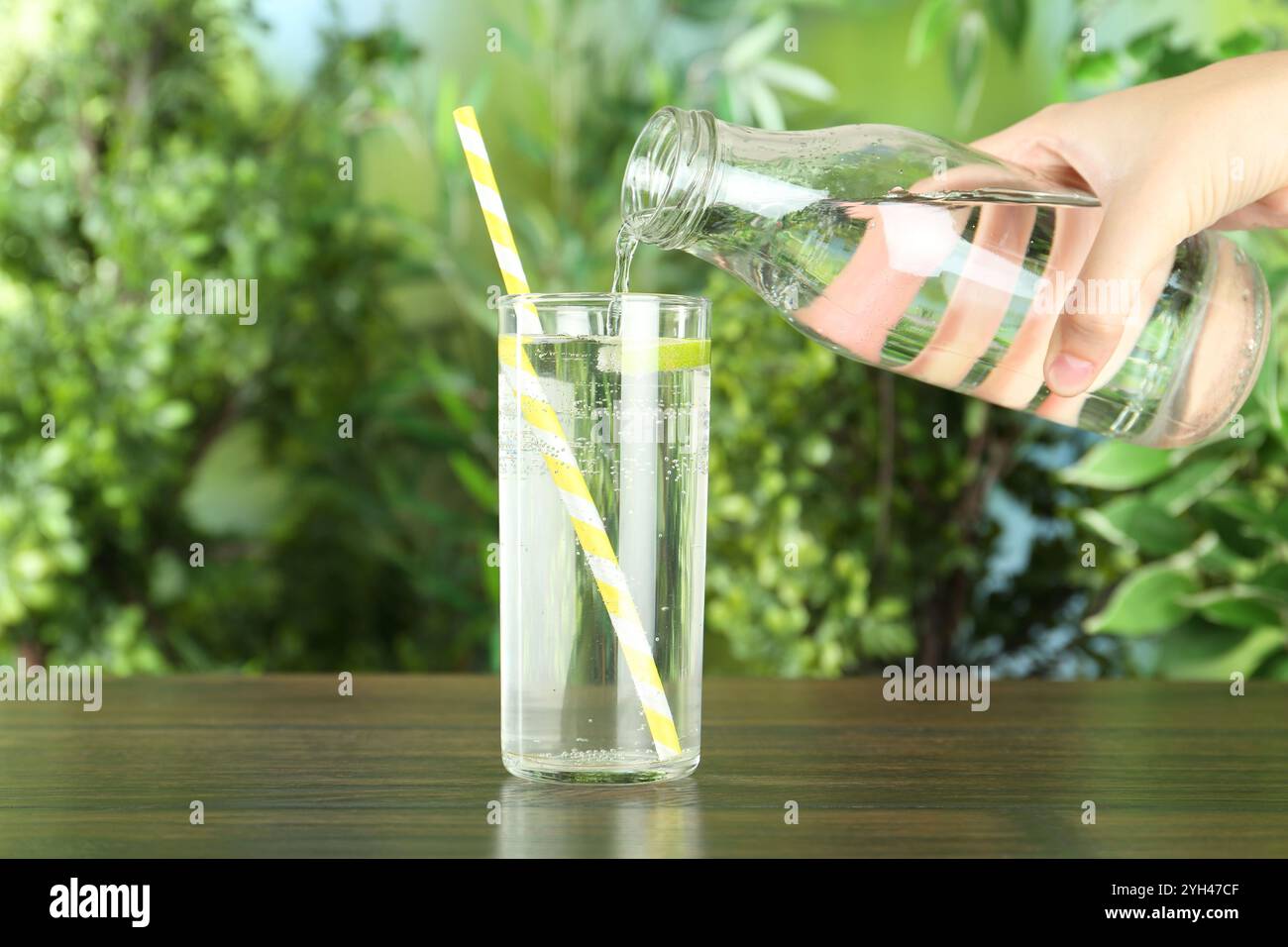 Woman pouring soda water from bottle into glass at wooden table ...