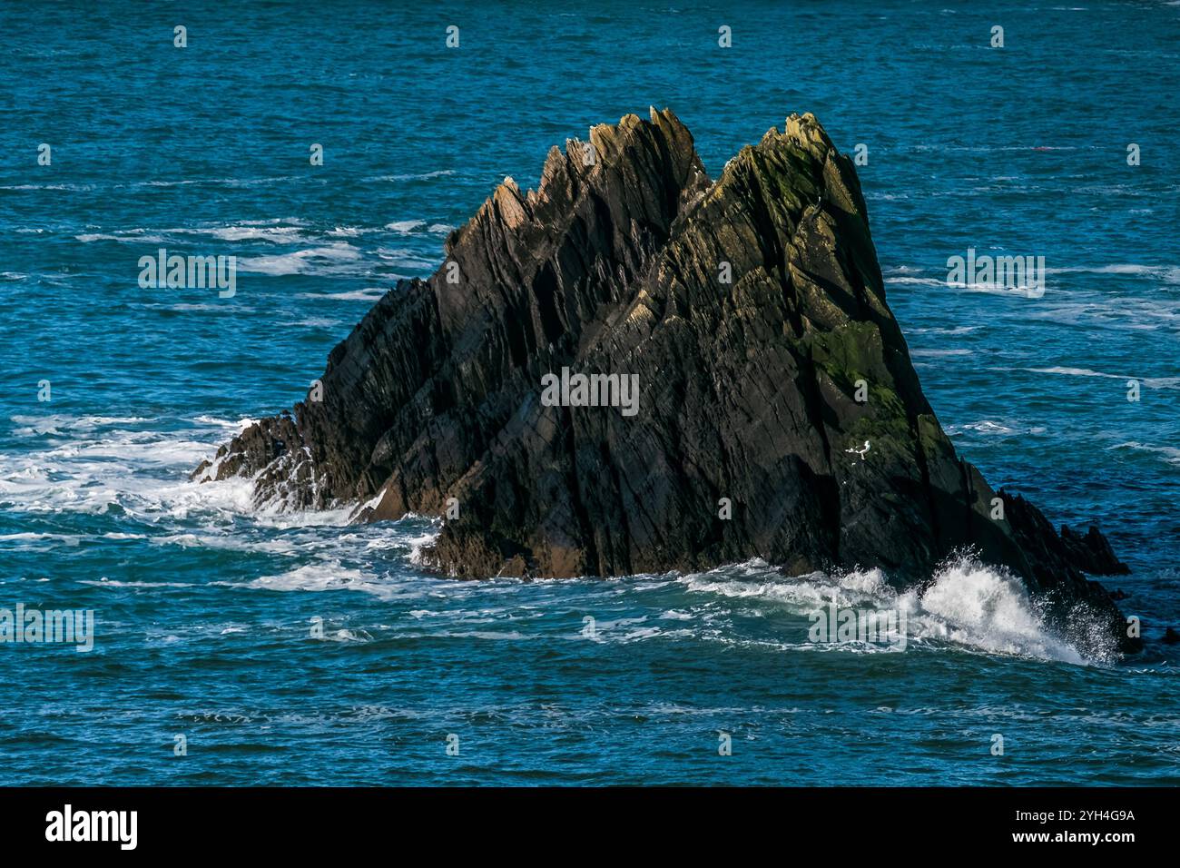 A dramatic rock formation juts out from the ocean, surrounded by ...