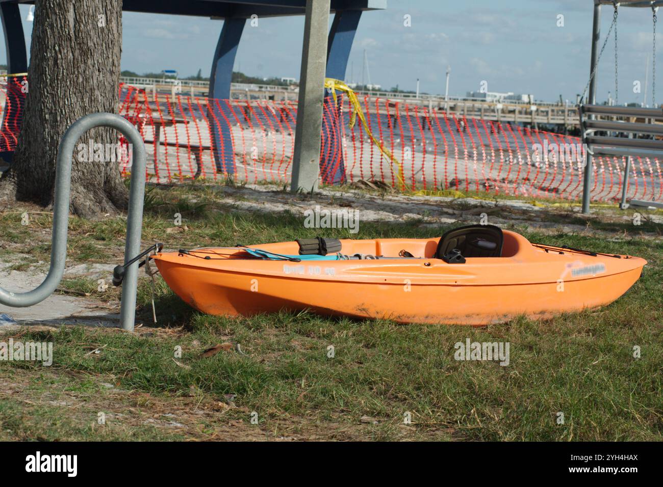 Isolated orange kayak in grass edge of beach chained to a metal bike ...