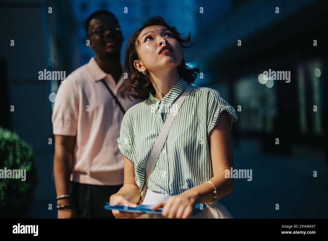 Two young people exploring the vibrant city at night, gazing in awe and ...