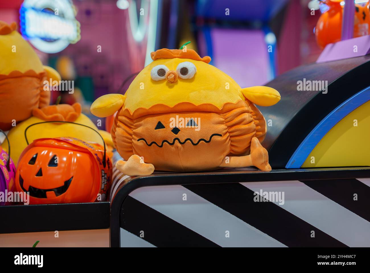 A plush toy resembling a pumpkin with a jack o' lantern face sits on a ...