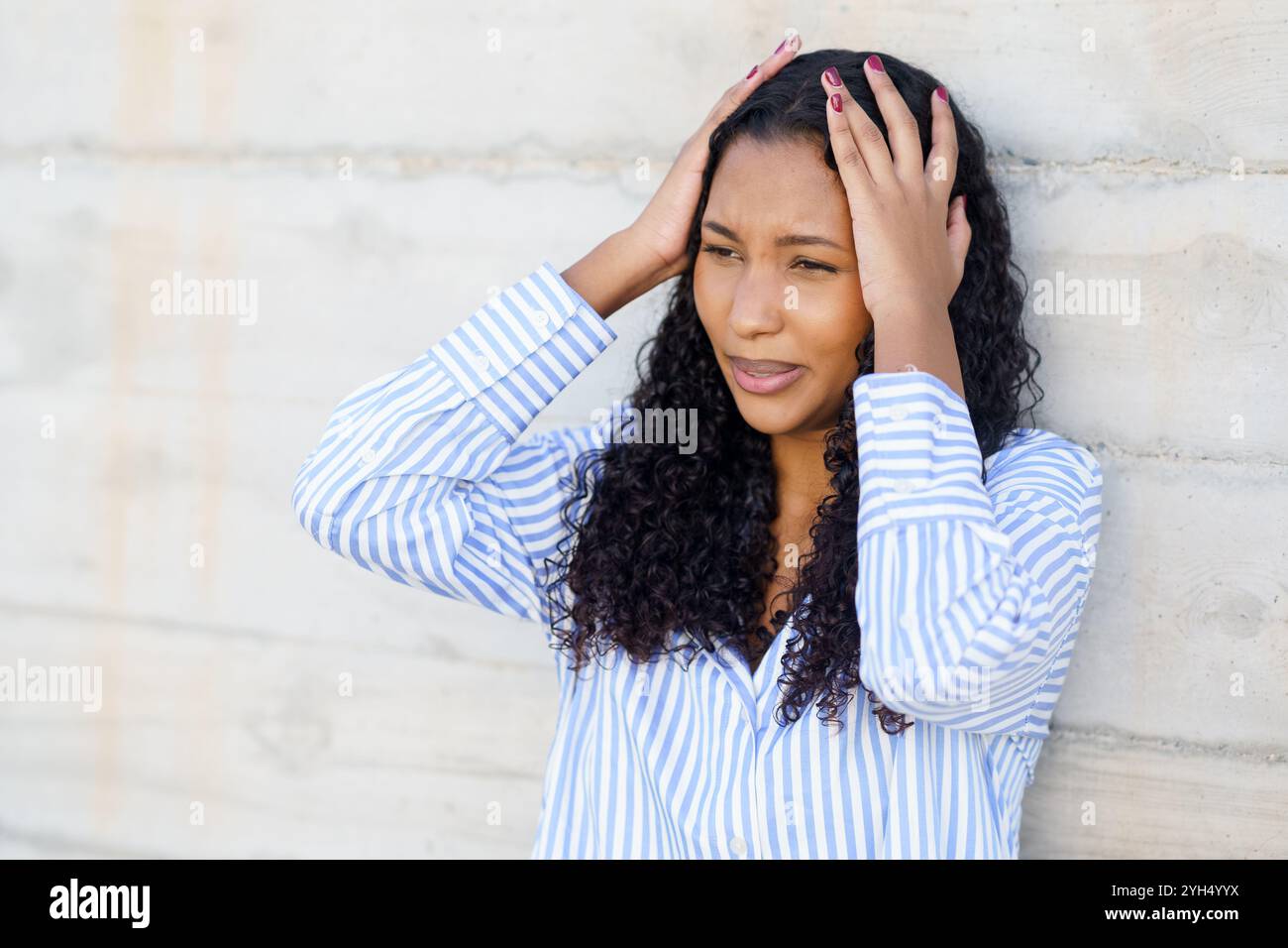 A Stressed Young Woman is Holding Her Head in Discomfort Against a Wall ...