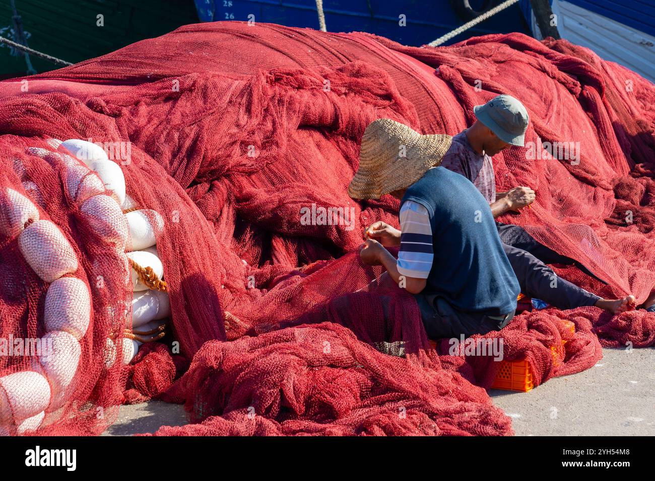 Two Fishermen repairing a red fishing net at a sea port. Essaouira ...
