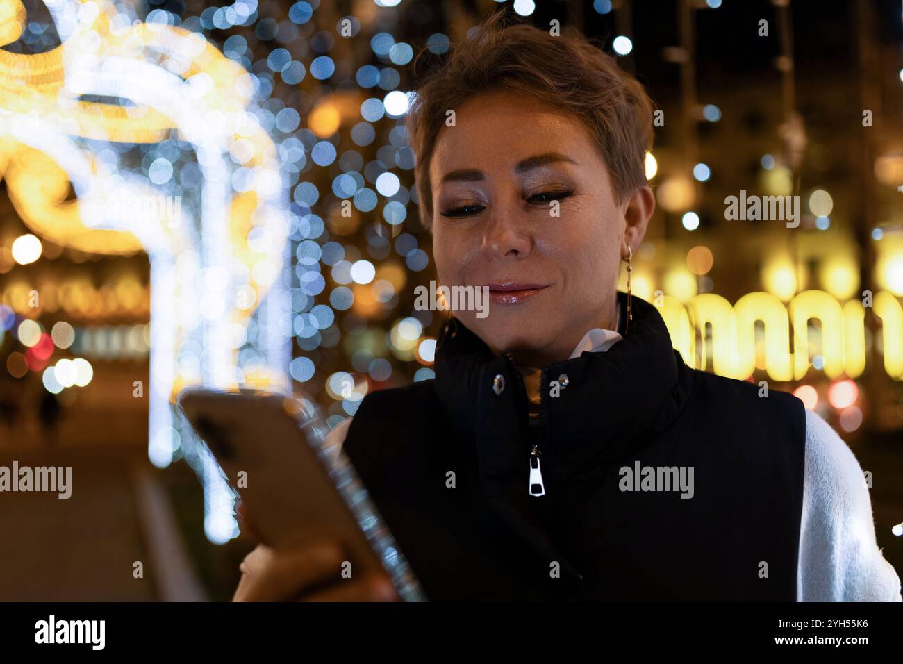 A woman walks through the city at night, checking her phone Stock Photo ...