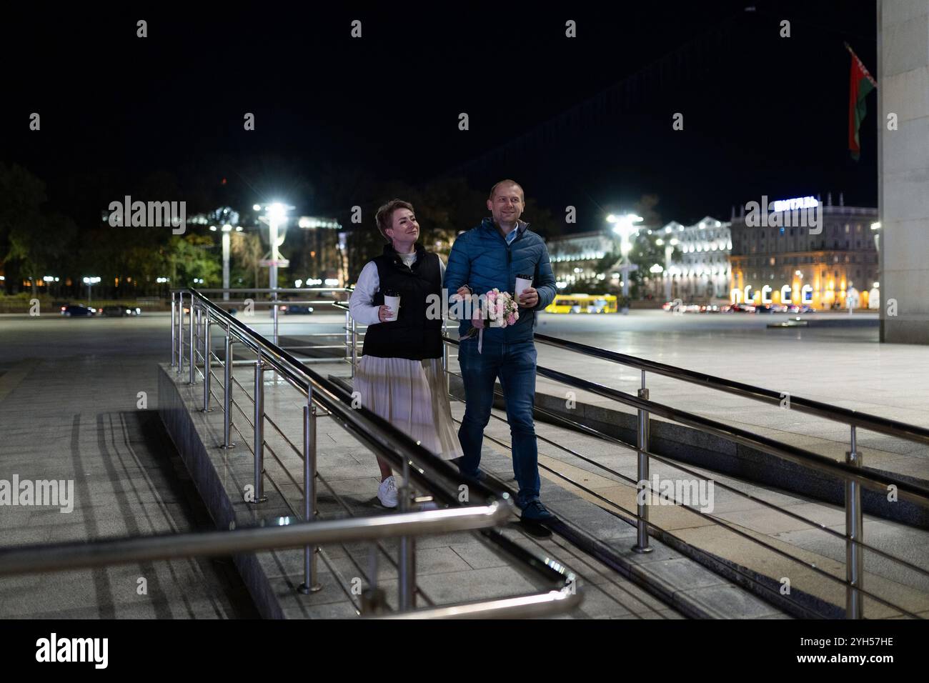 A couple walks arm-in-arm through the city at night, enjoying a stroll ...