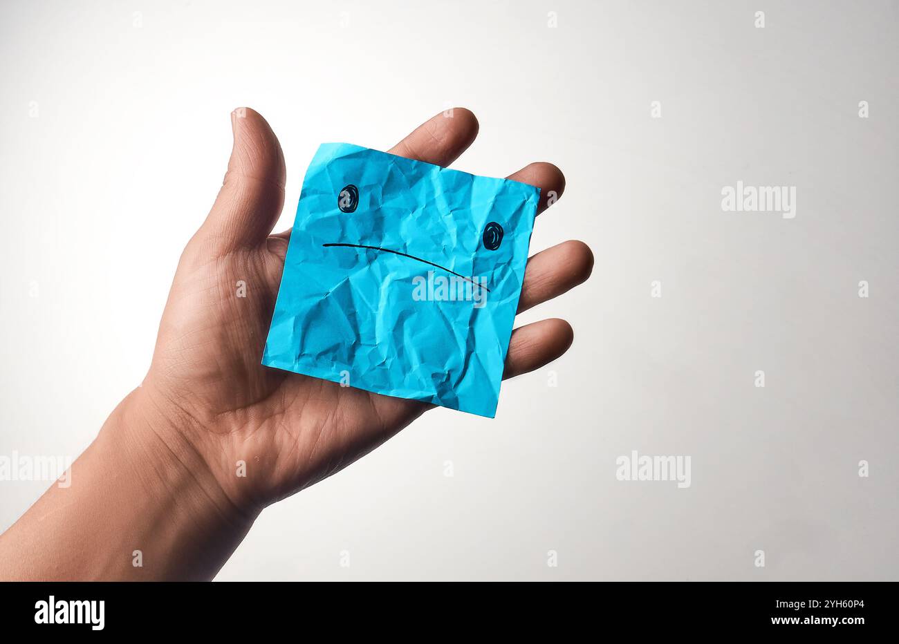 Hand of a Latin man holding a sad blue paper face on a white background ...