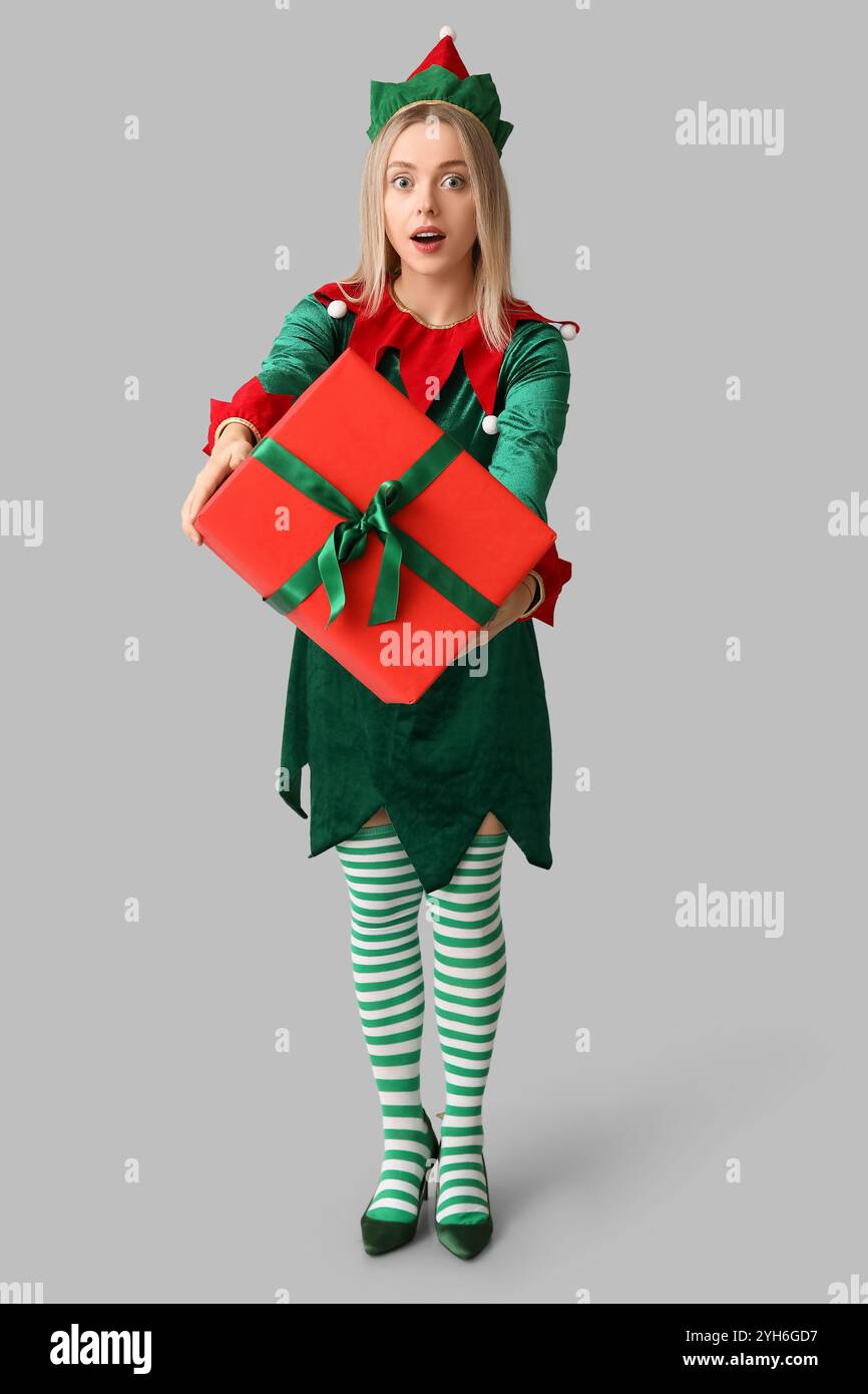 Emotional young woman in elf costume with Christmas gift box on white ...