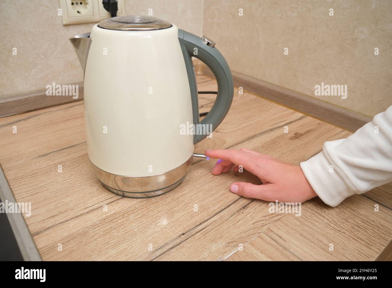Hand pressing button on electric kettle on wooden kitchen countertop ...