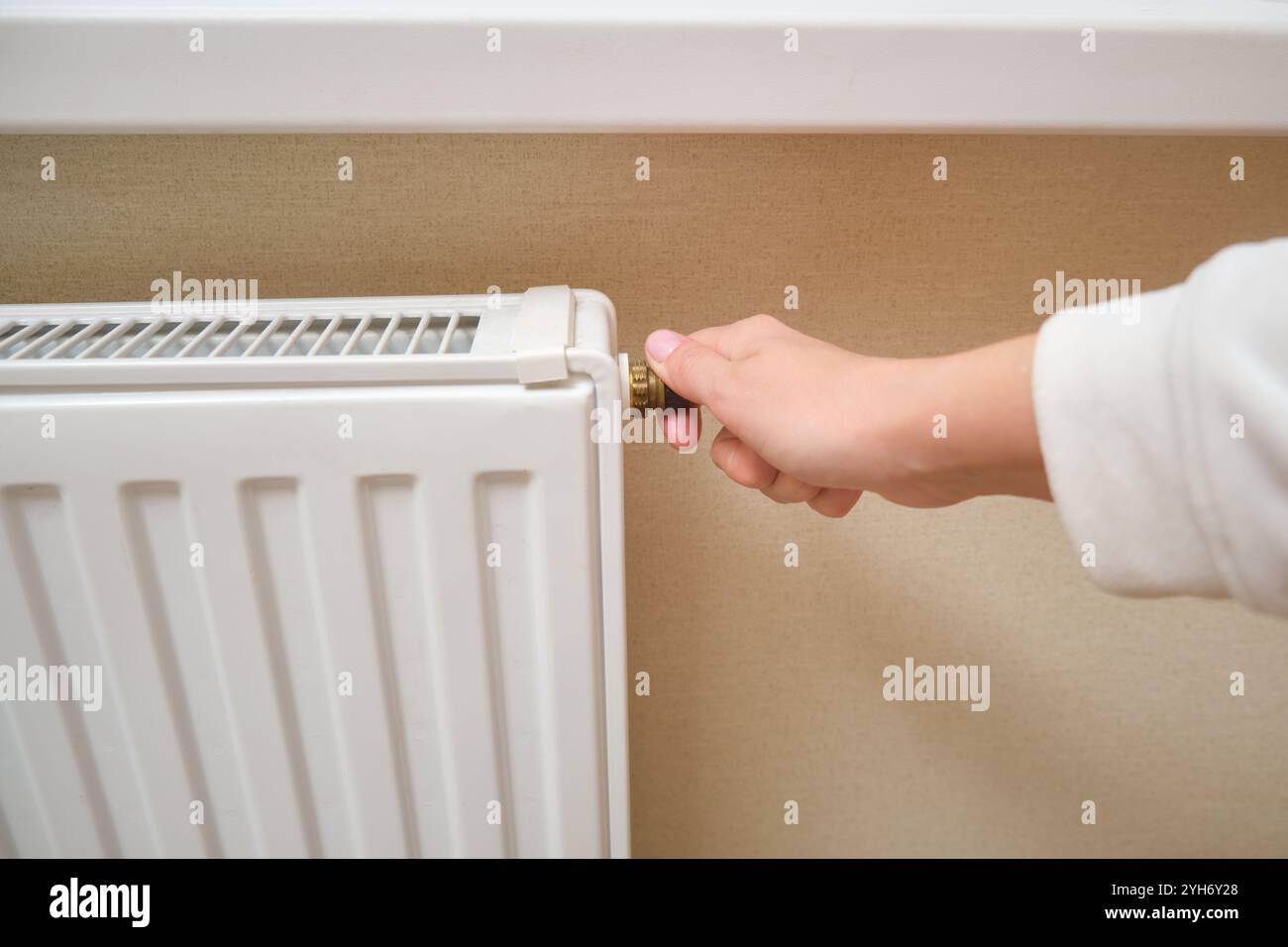 Hand adjusting radiator valve on beige wall background. Close-up of ...