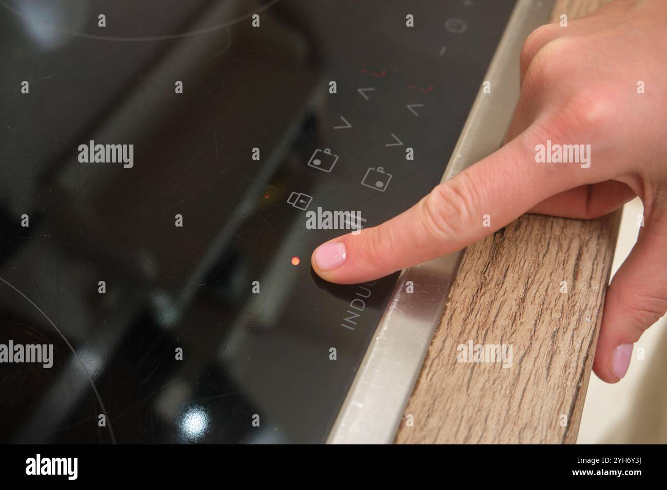 Finger pressing button on induction cooktop control panel with ...