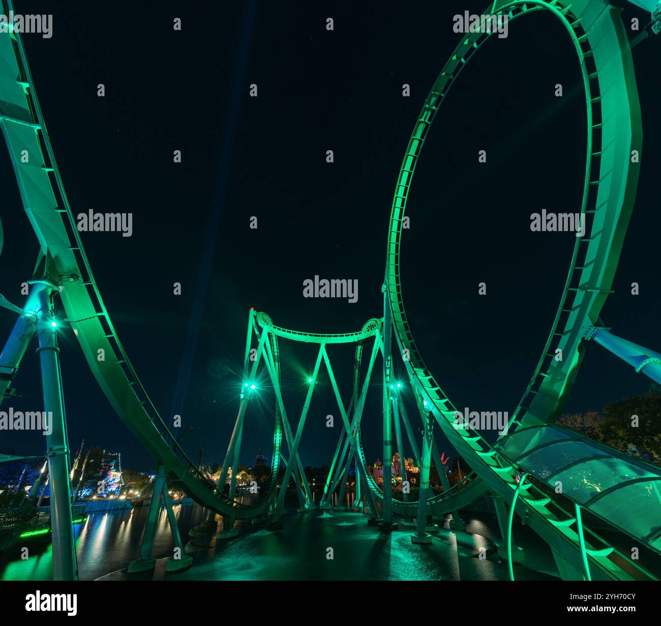 A vibrant green-lit roller coaster against the night sky with loops and ...