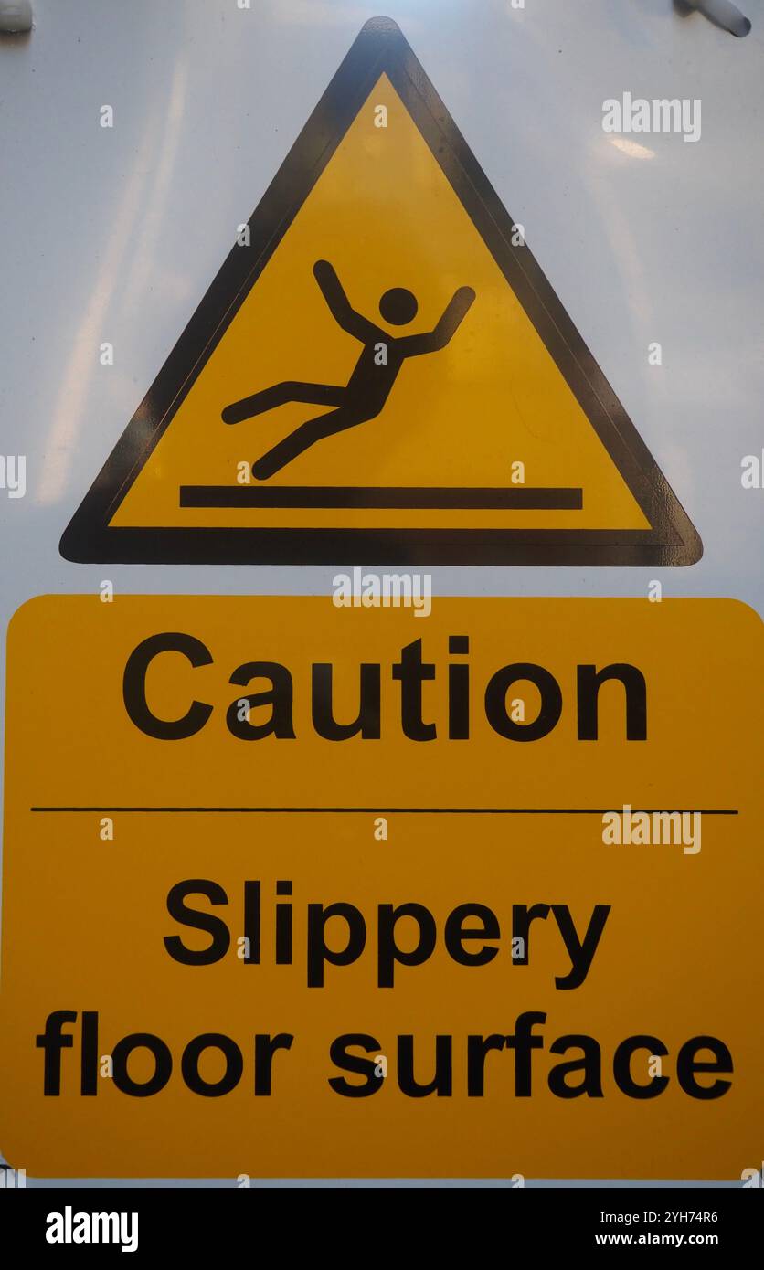 Yellow and black triangular sign warning of slippery floor surface with ...