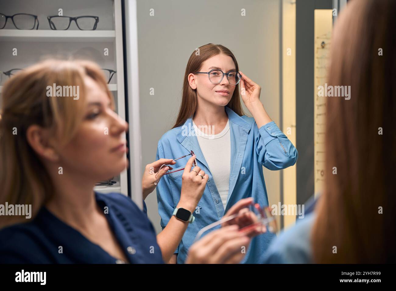 Customer adjusting glasses while optician observes Stock Photo - Alamy