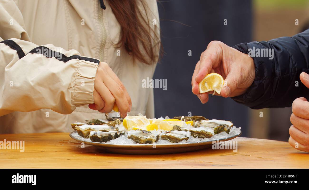 Midsection of two people eating oysters at outdoor farmers market at ...