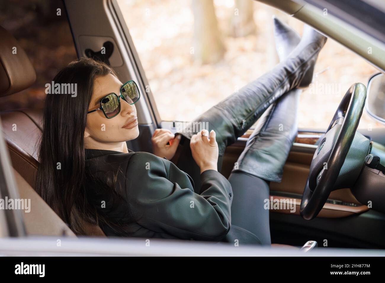 Stylish woman in sunglasses lounging in a car with legs up in leather ...