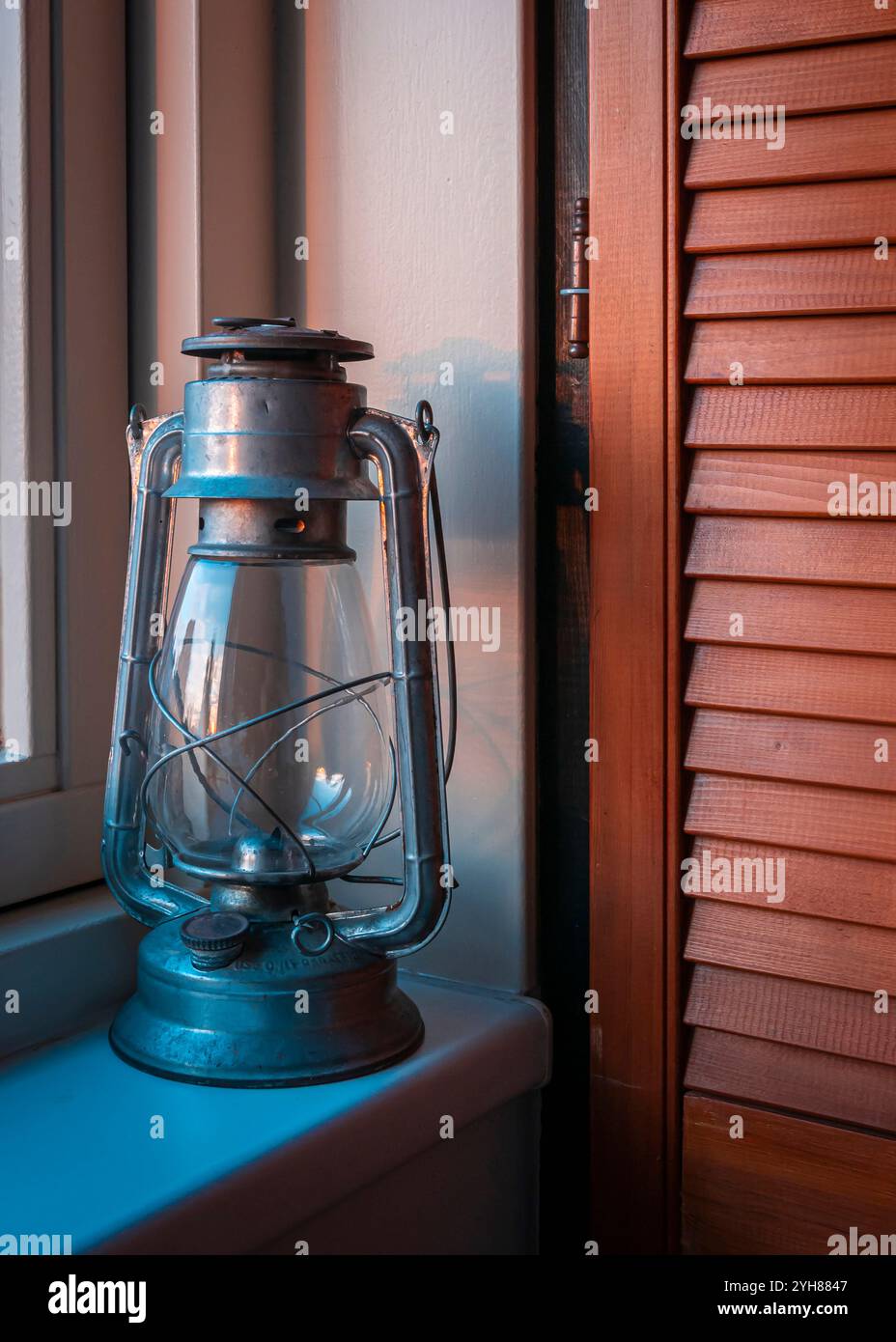 An old kerosene lamp on a windowsill in the rays of the setting sun ...